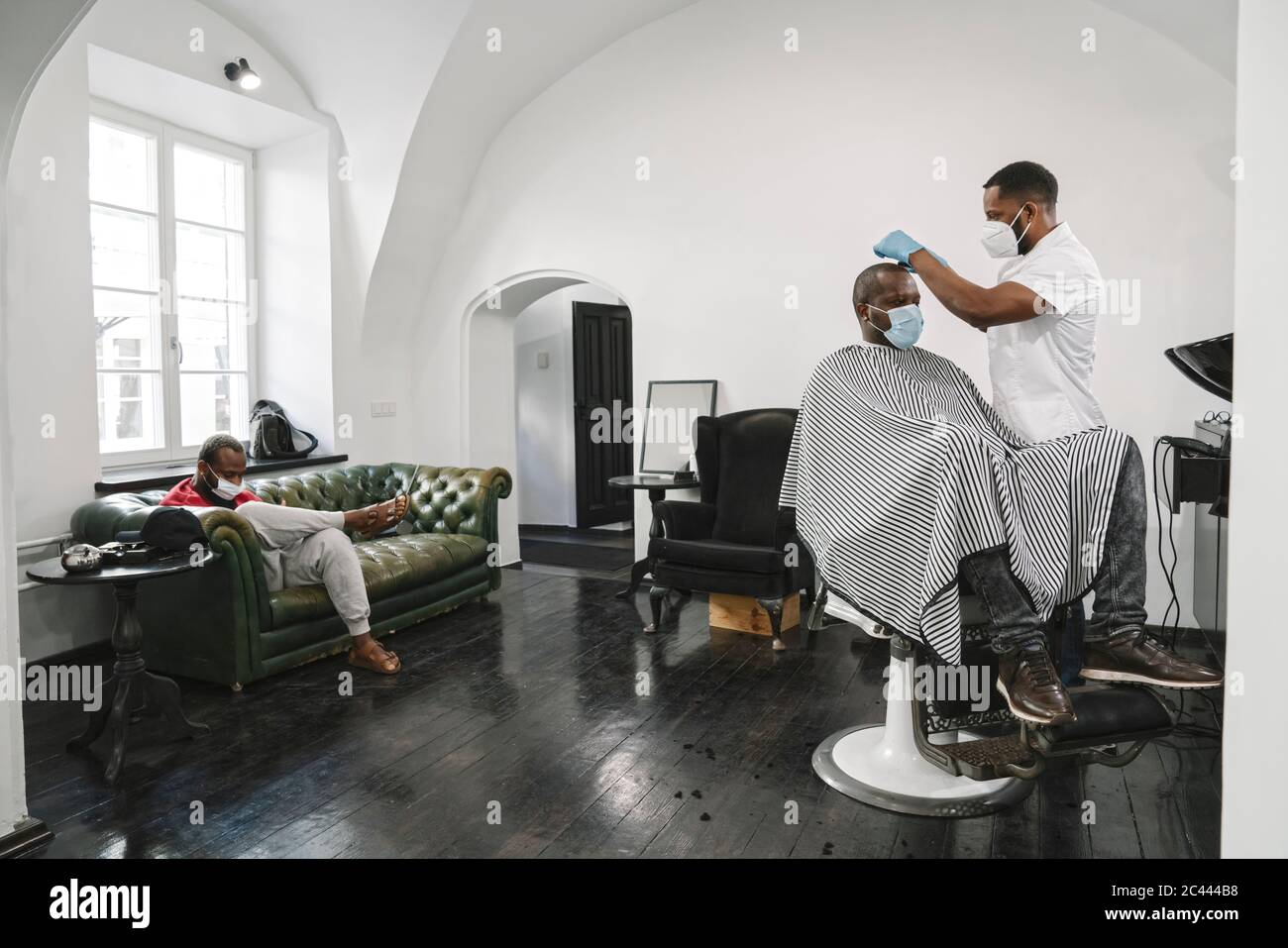 Barber wearing surgical mask and reusable gloves cutting hair of the ...
