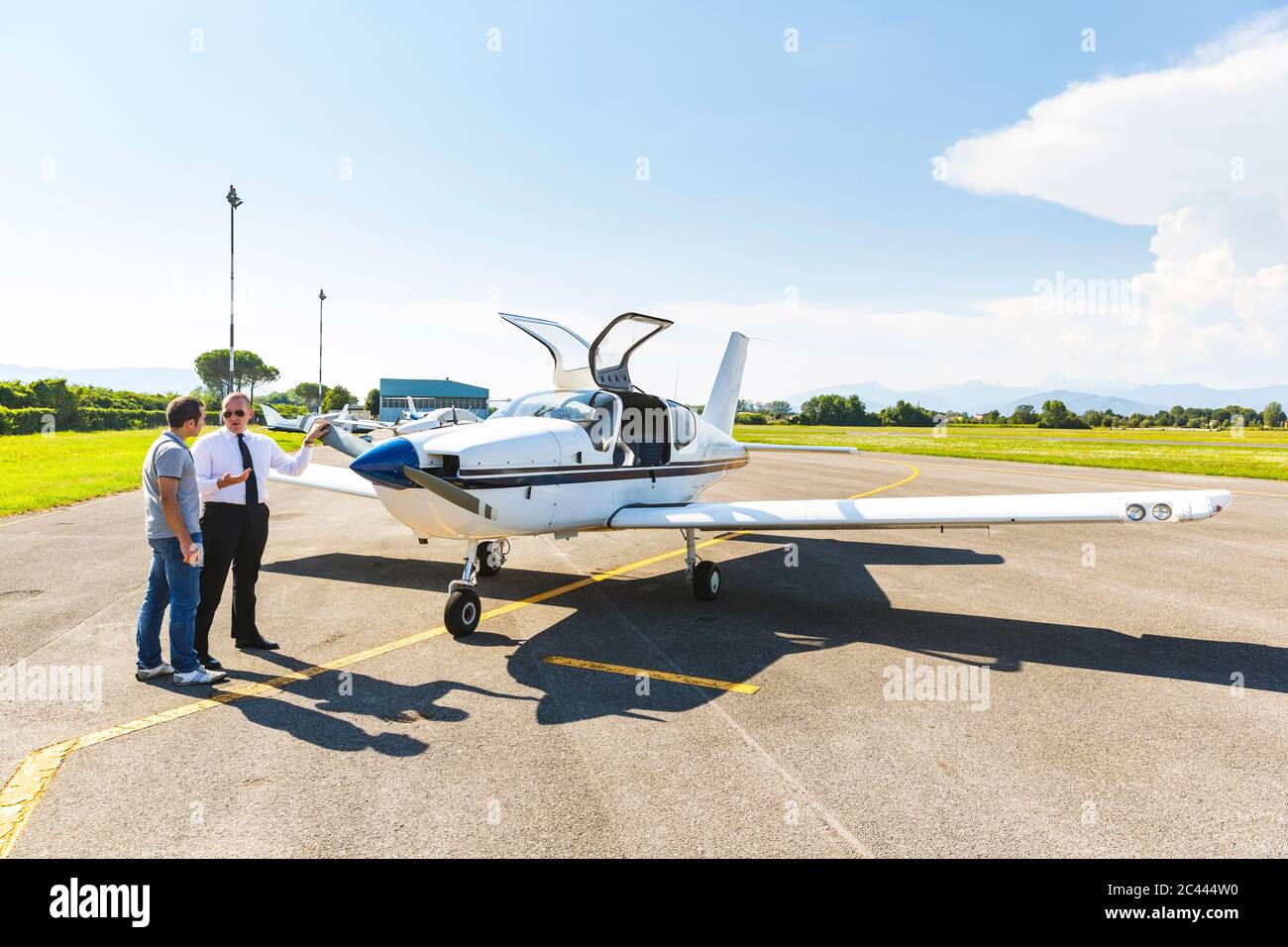 Pilot and Co-pilot satning on runway, talking in front of sports plane ...