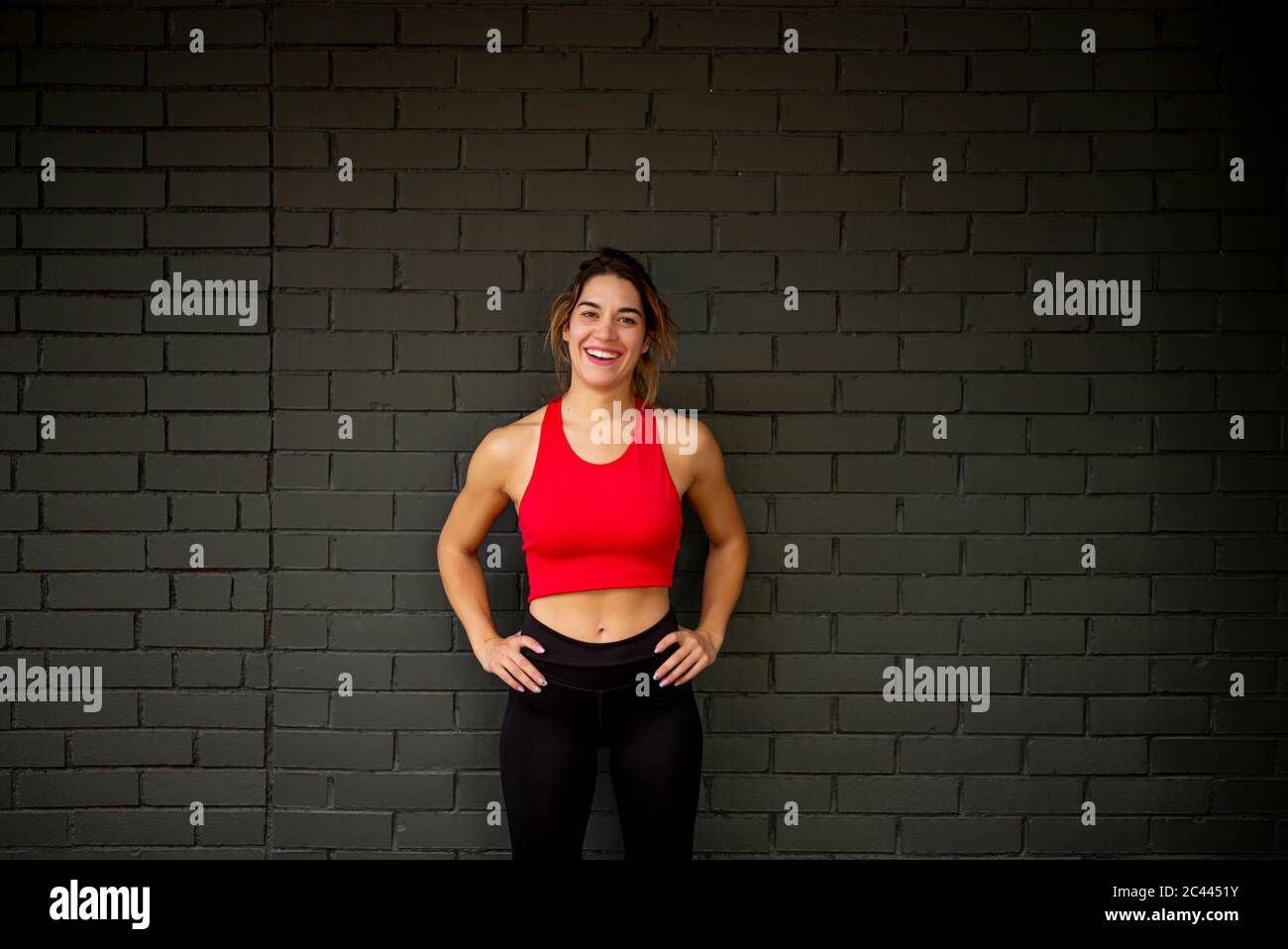 Smiling confident female athlete with arms akimbo standing against ...