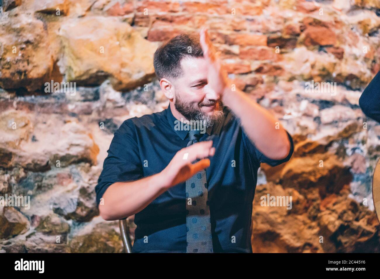 Bearded smiling singer clapping hands while singing against wall in ...