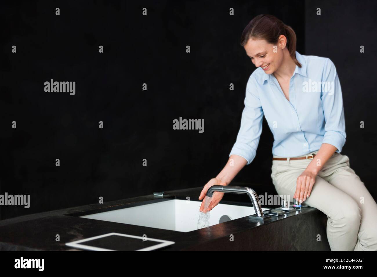 Smiling mid adult woman washing hands in modern bathroom sink Stock ...