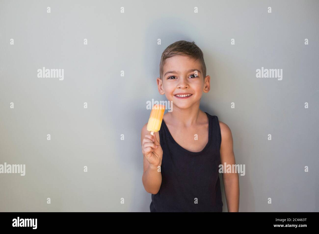 Portrait of cute smiling boy eating popsicle while standing against ...