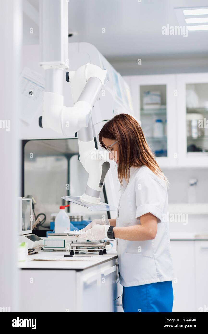 Mature female scientist using equipment while working at desk in ...