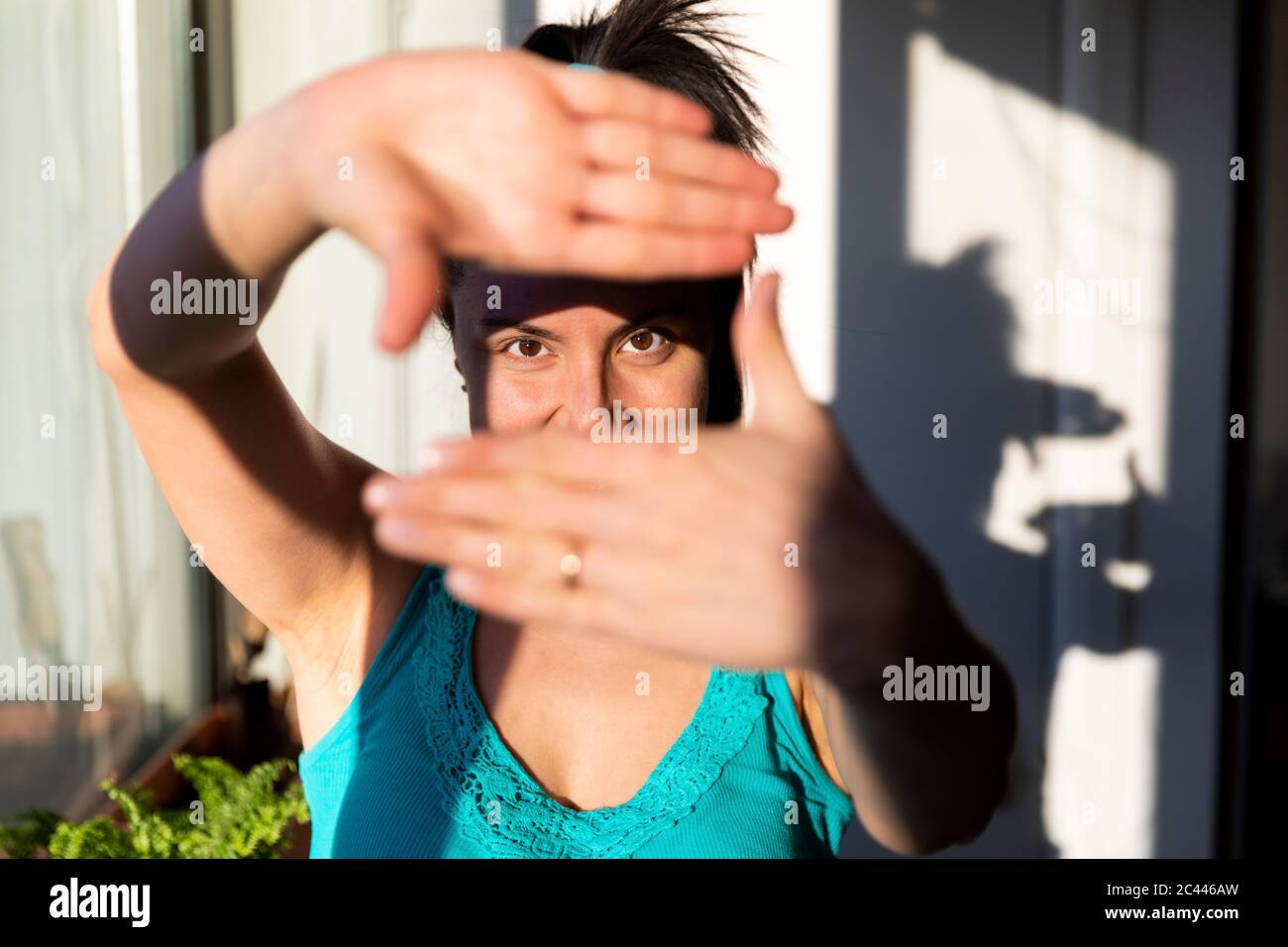 Woman standing by window, looking through finger frame Stock Photo - Alamy