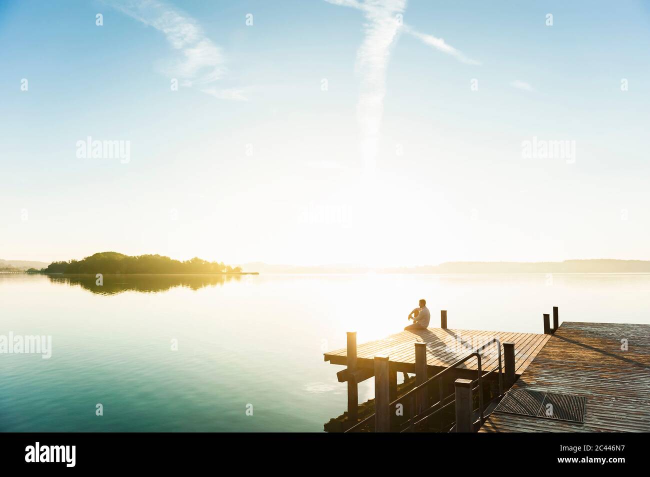 Young man sitting on jetty at lake enjoying sunrise Stock Photo - Alamy