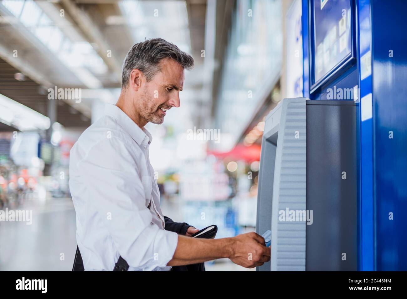Businessman withdrawing money through ATM machine at railroad station ...