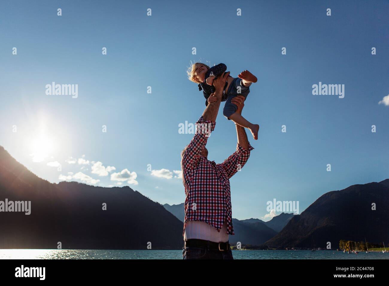 Father holding aloft daughter against blue sky achensee hi-res stock ...