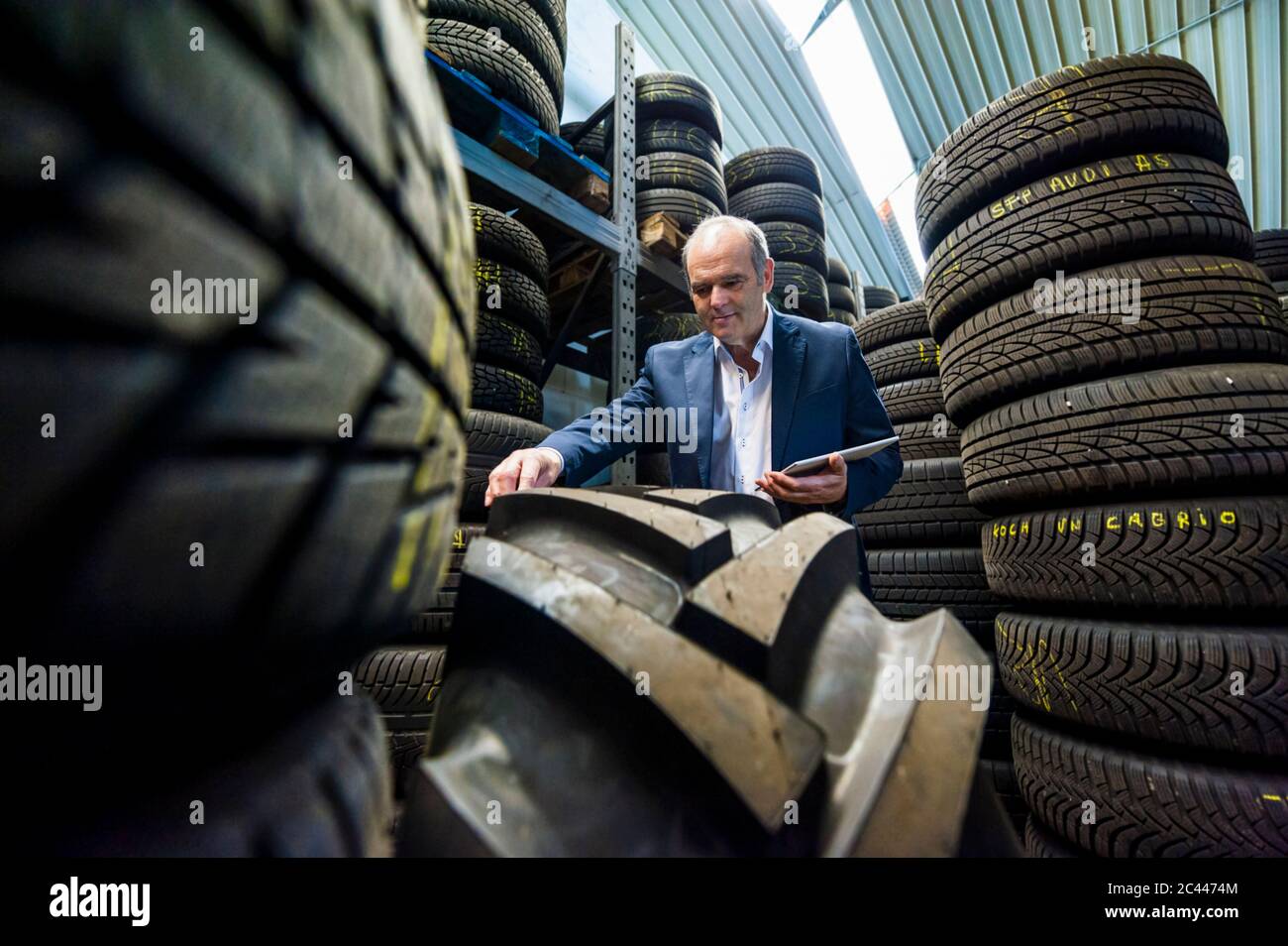 Senior male owner examining rubber tire at store Stock Photo - Alamy