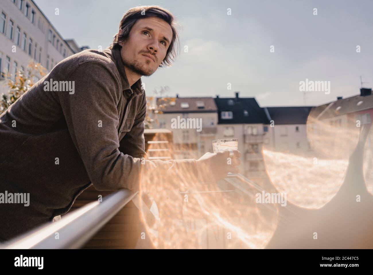 Man leaning on balcony railing, having a drink Stock Photo - Alamy