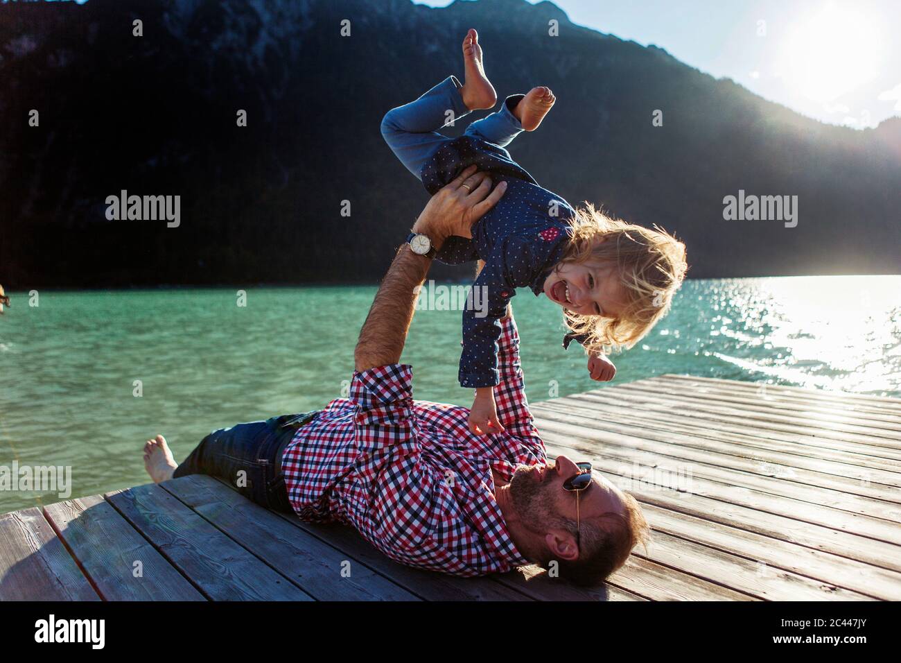 Father holding aloft happy daughter while lying on boardwalk by lake at ...