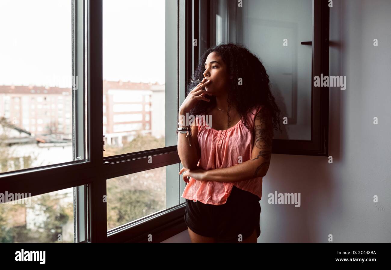 Young woman smoking a cigarette at the window Stock Photo - Alamy