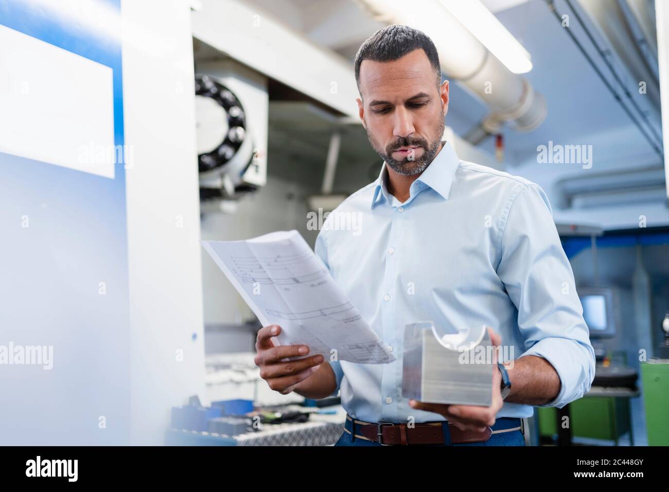 Businessman holding plan and workpiece in factory hall Stock Photo - Alamy