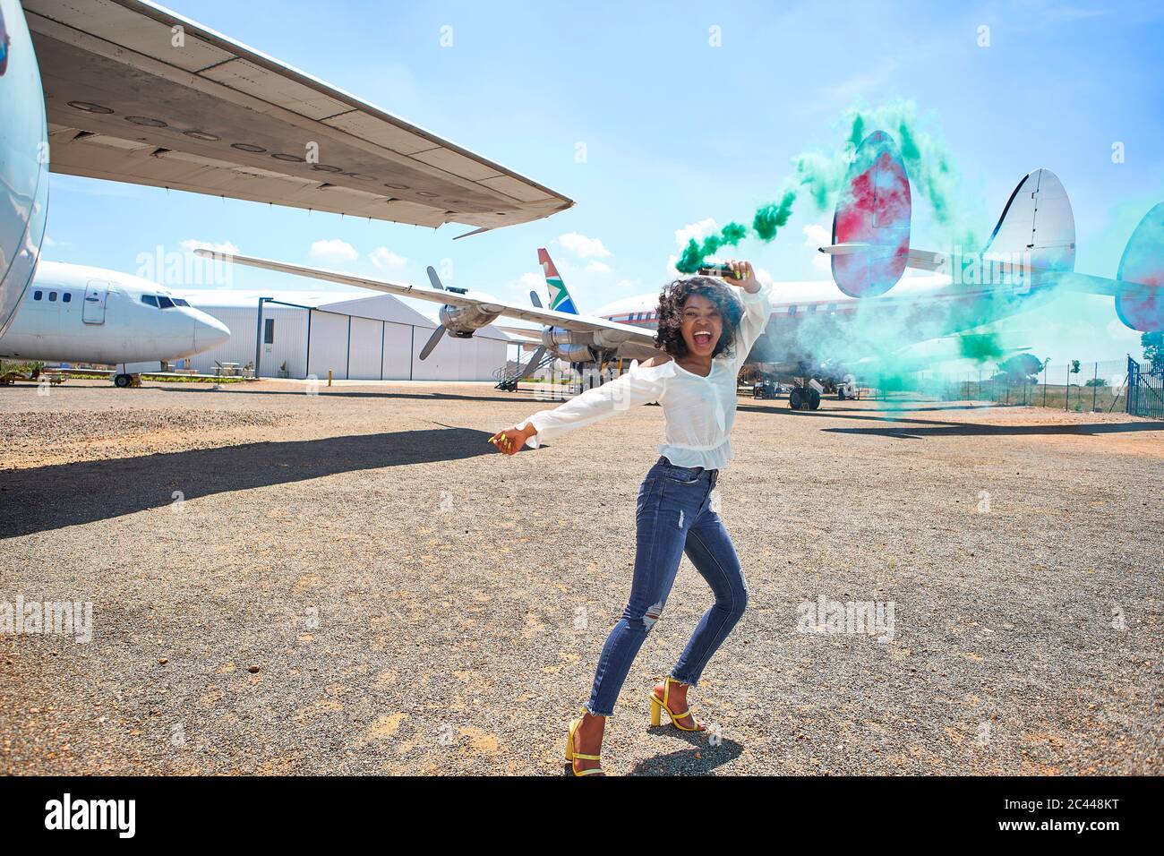 Cheerful young woman dancing with distress flare at airport runway on ...