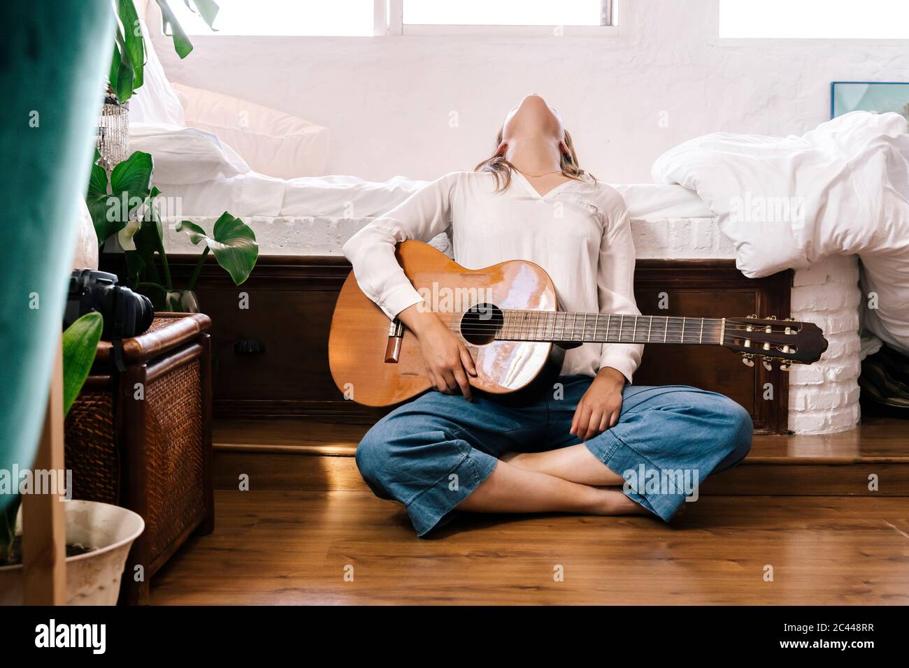 Woman with guitar sitting on the floor in front of bed leaning back ...