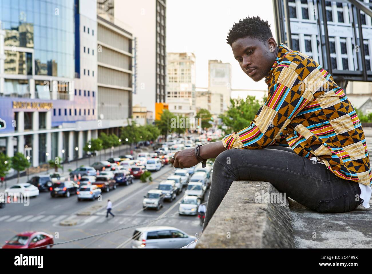 Young man in patterned shirt sitting on roof terrace in the city ...