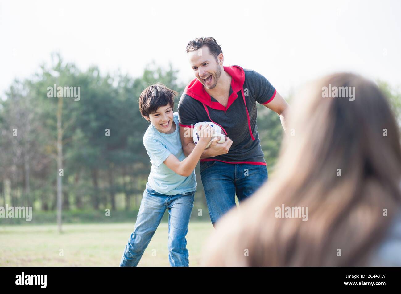 Cheerful father and son playing rugby with woman in foreground at park ...