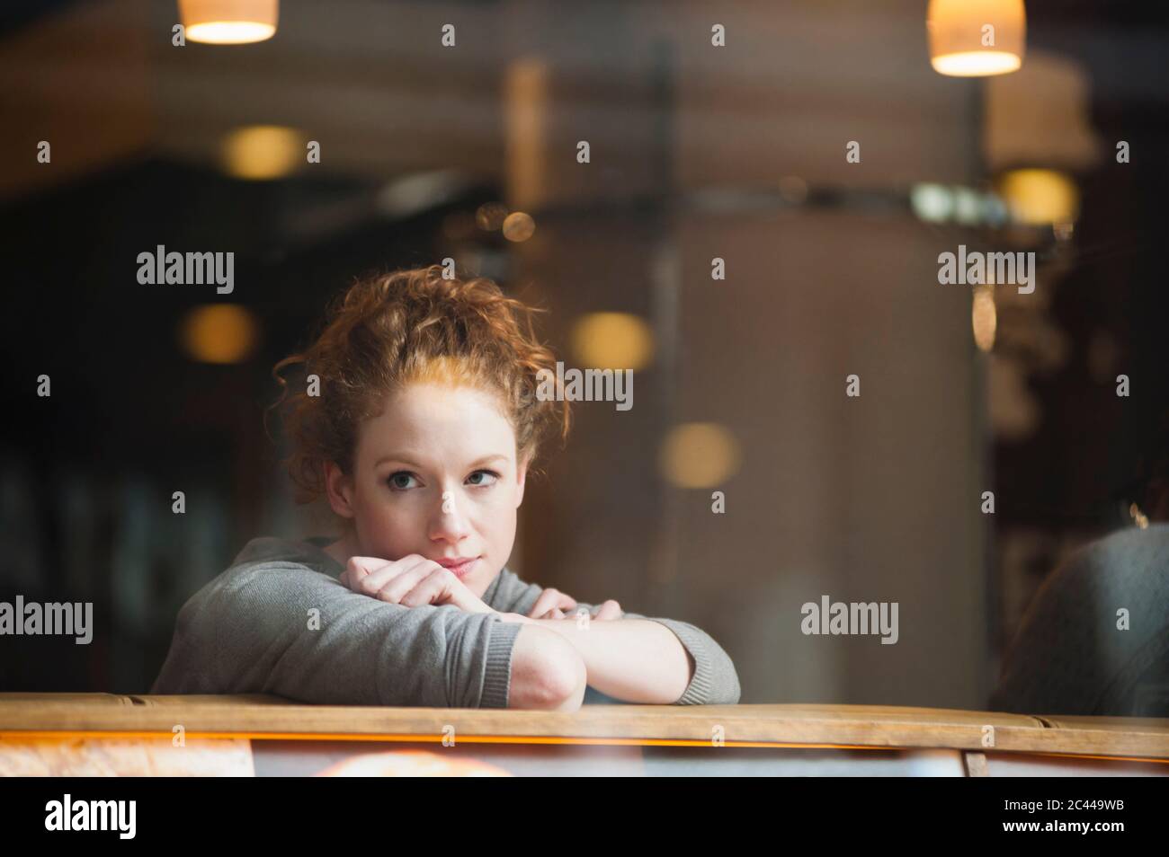 Thoughtful young woman leaning on table seen through glass window in ...