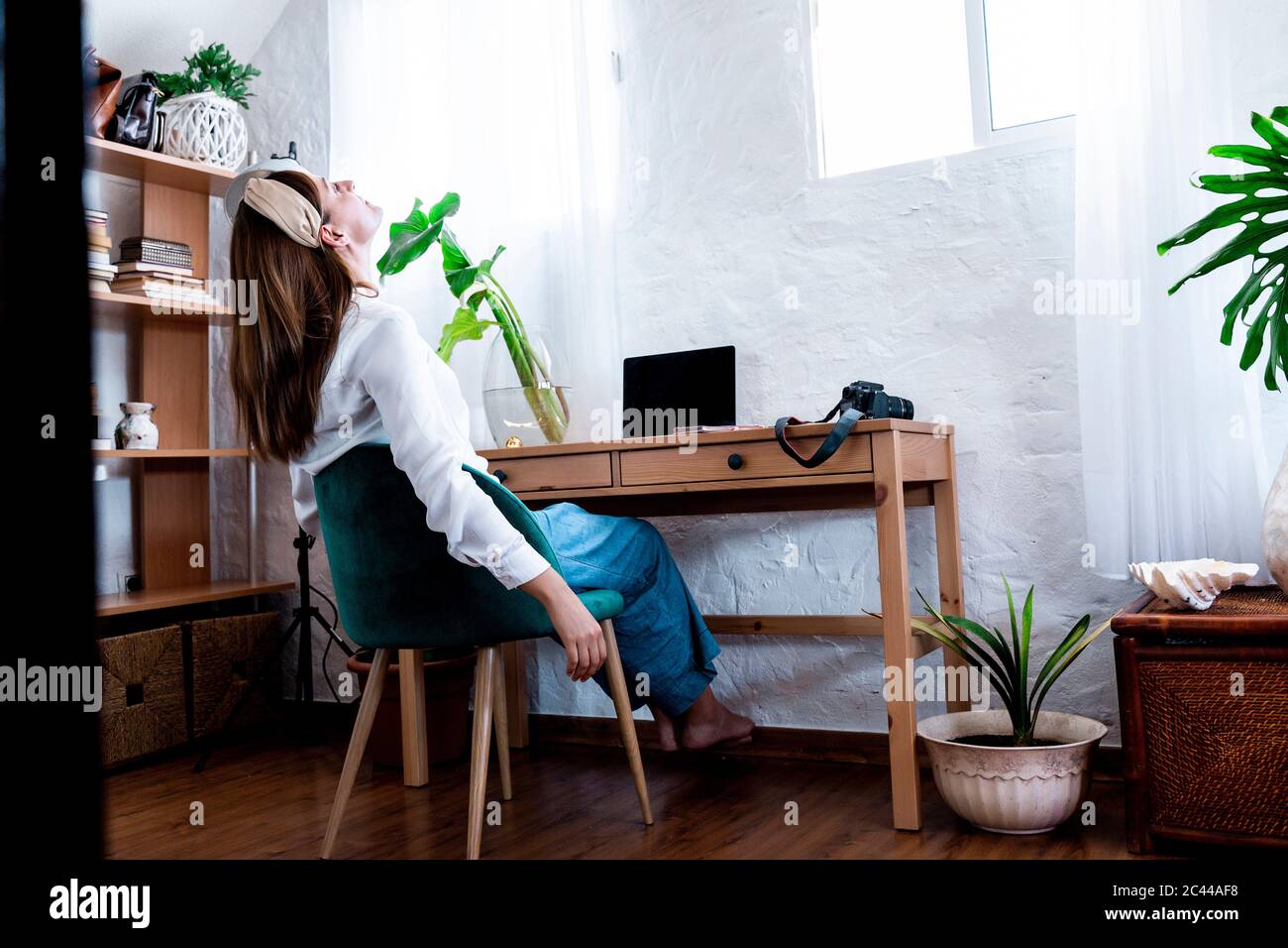 Tired woman looking up while sitting on chair with head back at home ...