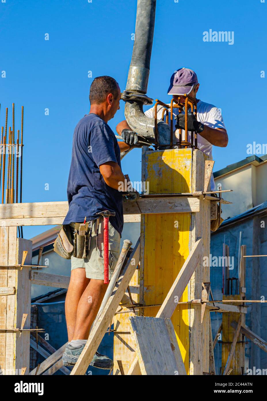 Worker pouring cement pouring into pillars formwork at building area in ...