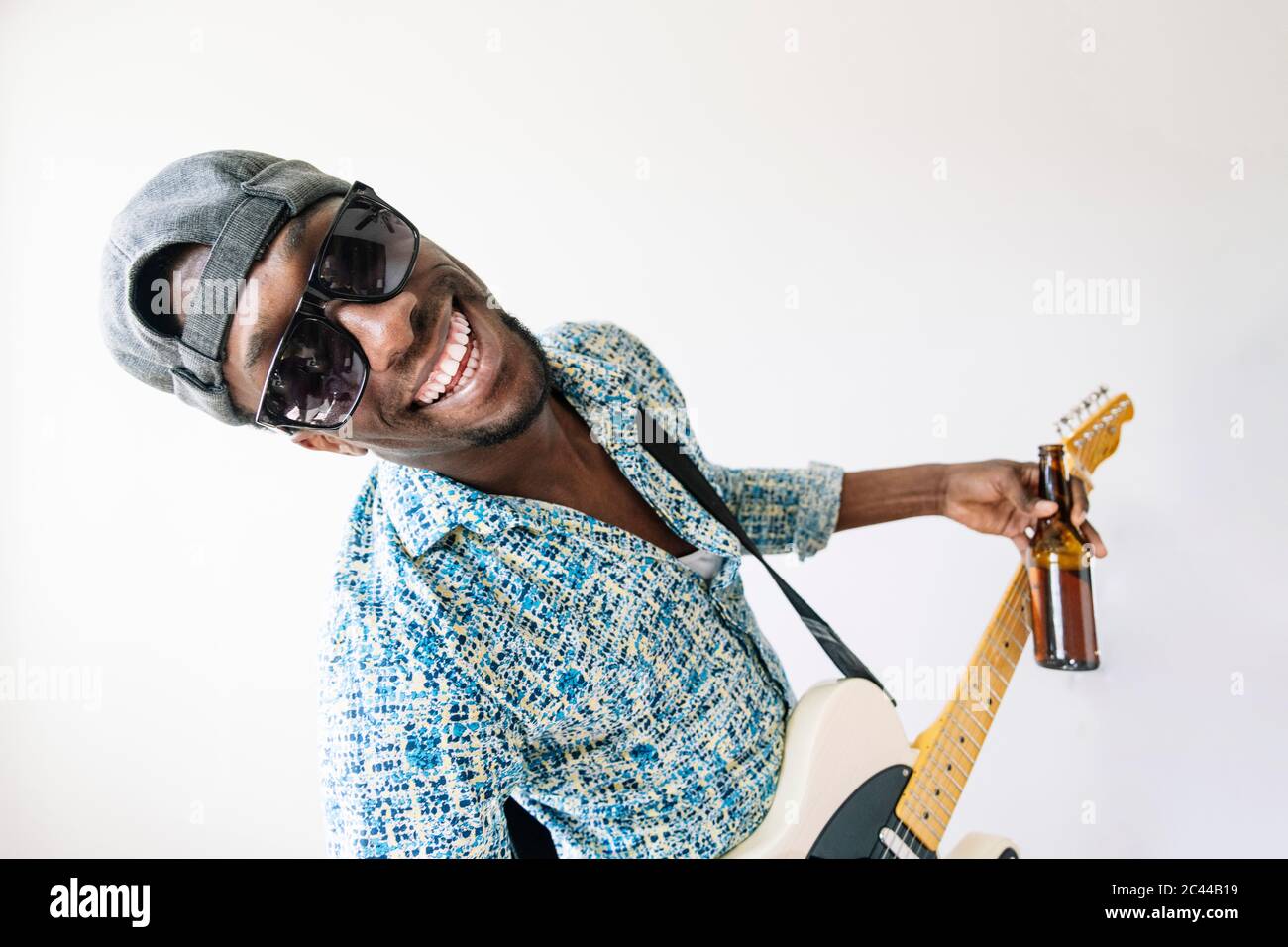 Portrait of smiling young musician holding guitar and beer bottle ...