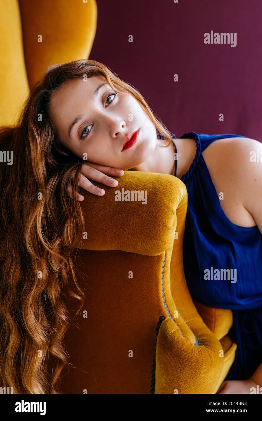 Portrait of confident young woman leaning on golden chair against ...
