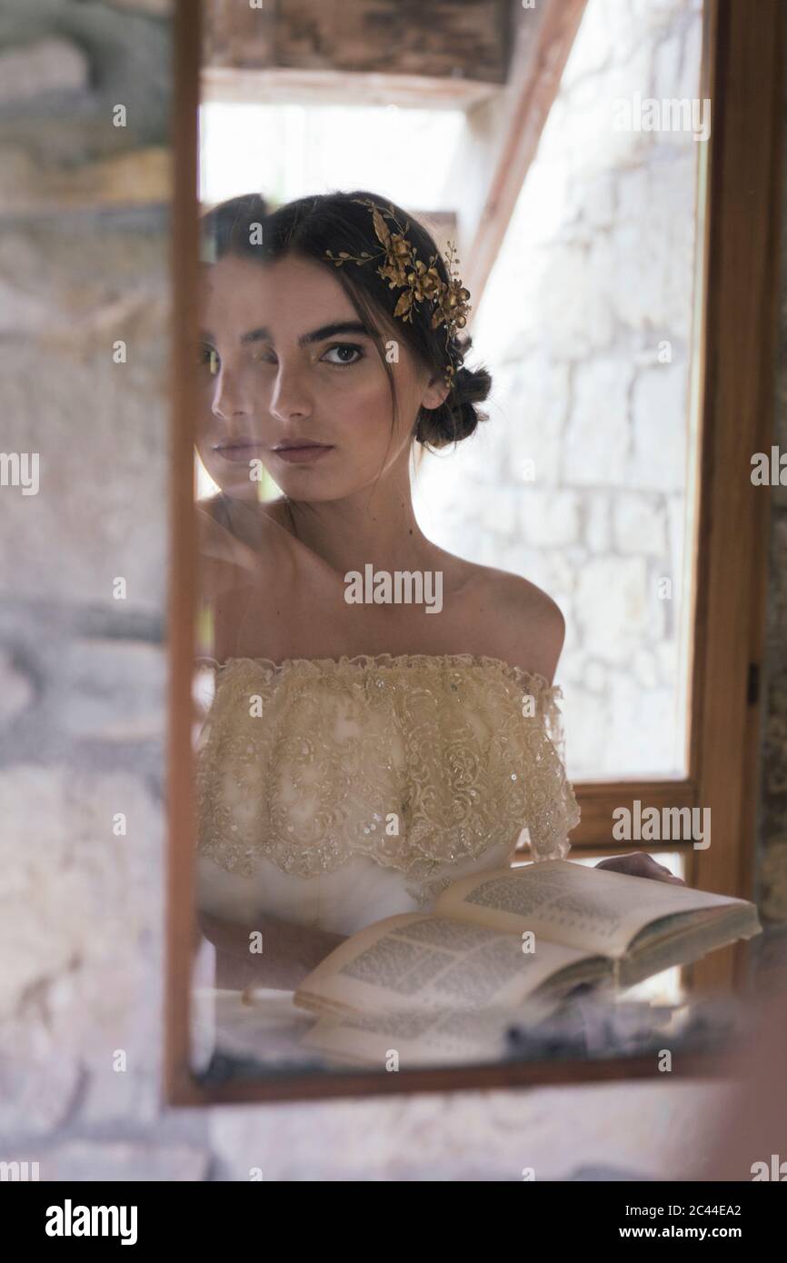 Young woman in wedding dress with book looking at mirror Stock Photo ...