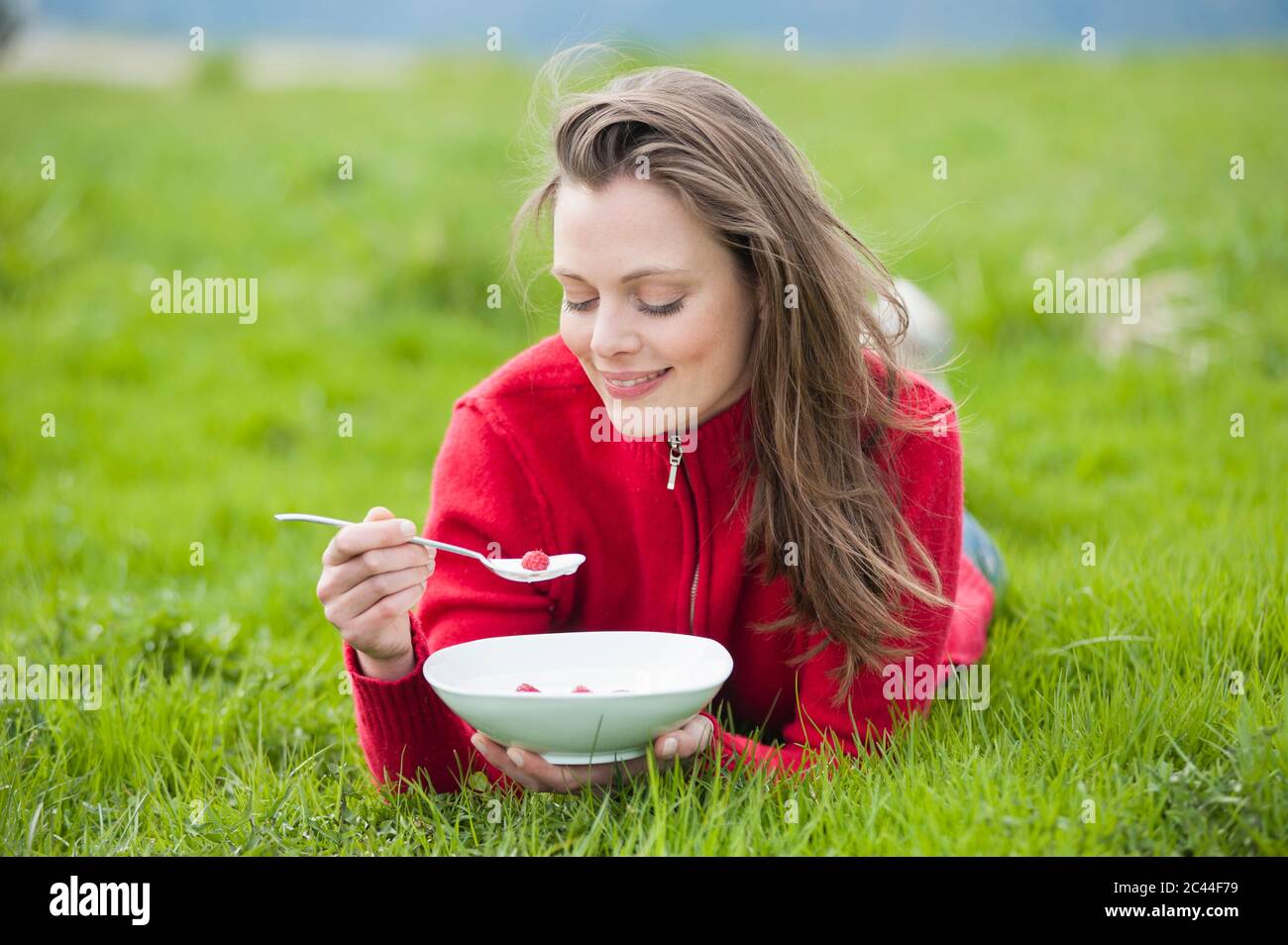 Smiling beautiful woman eating fresh yogurt and raspberry while lying ...