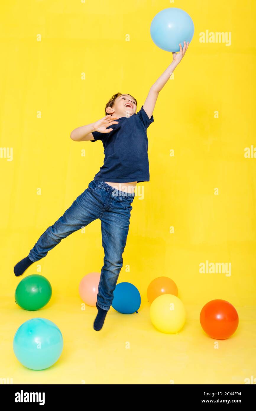 Full length of boy catching balloon while playing against yellow ...