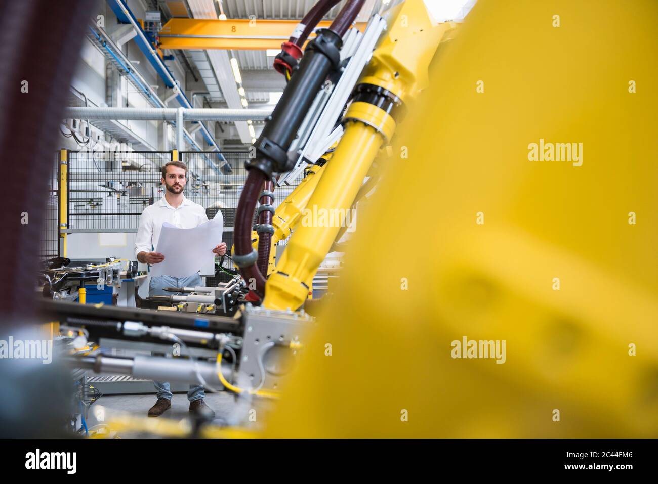 Confident young male engineer looking at robotic arm in factory Stock ...