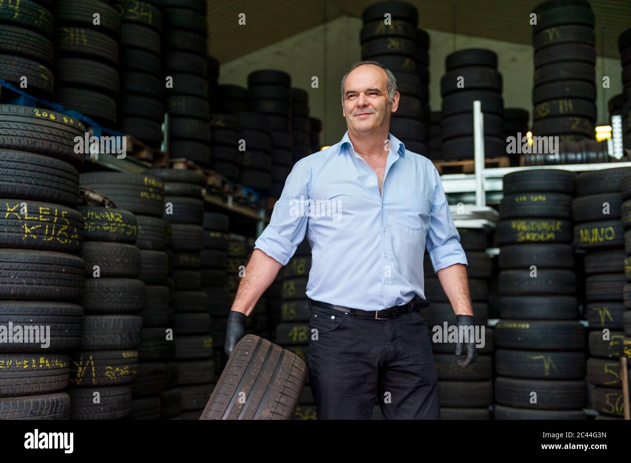Confident senior male owner holding tire while working at store Stock ...