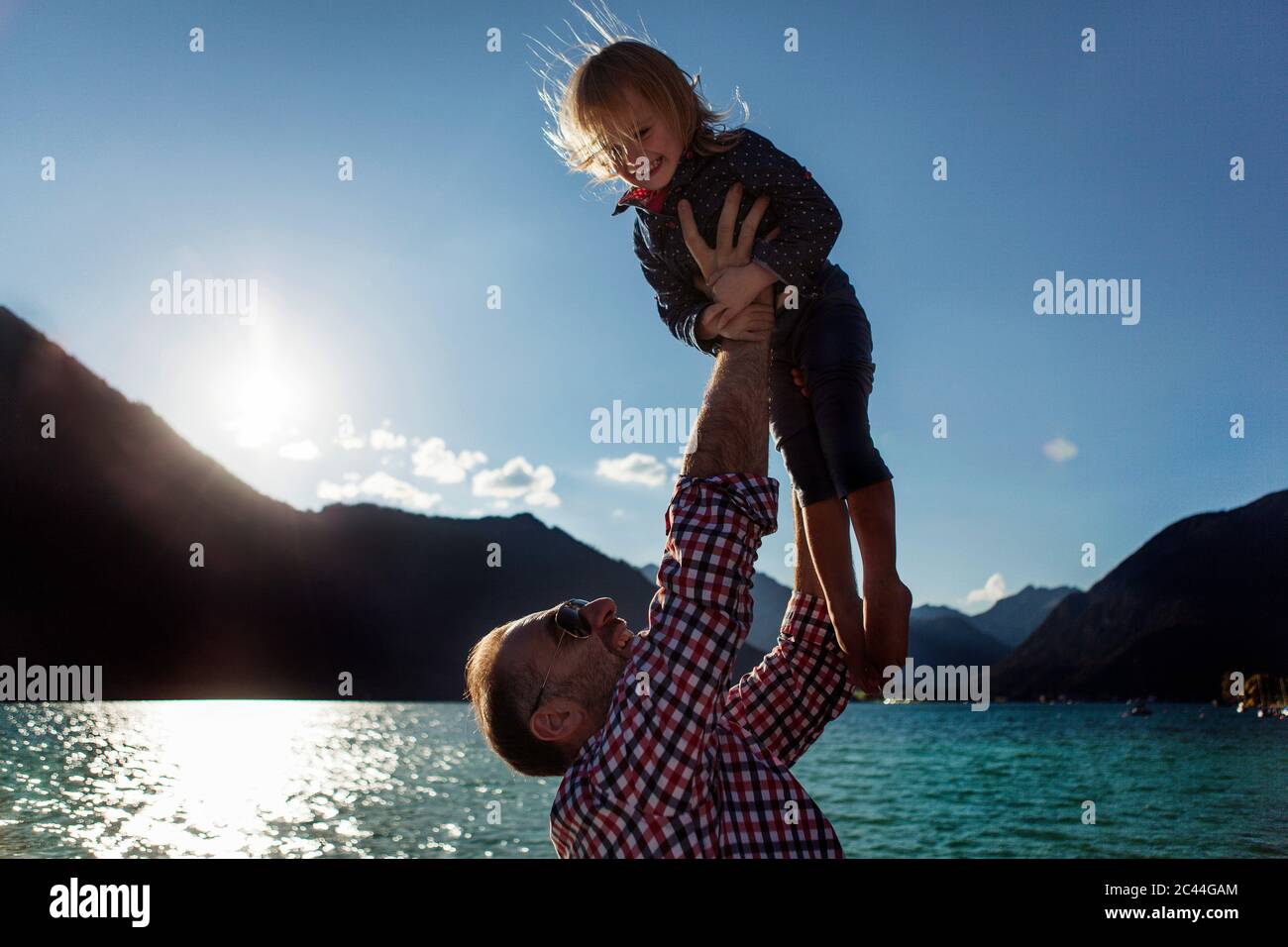 Father holding aloft cheerful daughter against blue sky achensee hi-res ...
