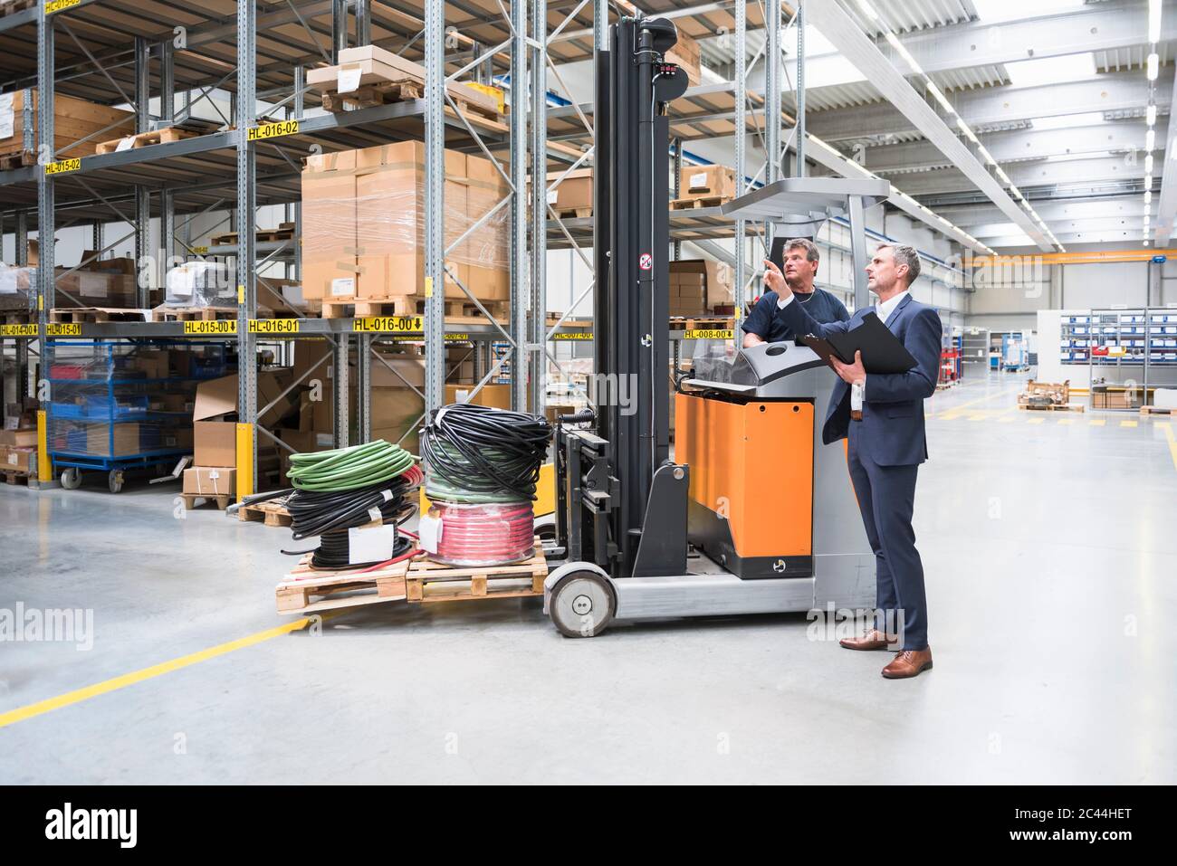 Businessman instructing worker on forklift in high rack warehouse Stock ...