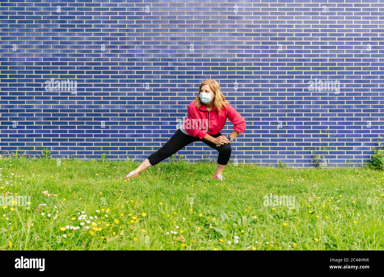 Woman with surgical mask stretching her leg on meadow Stock Photo - Alamy