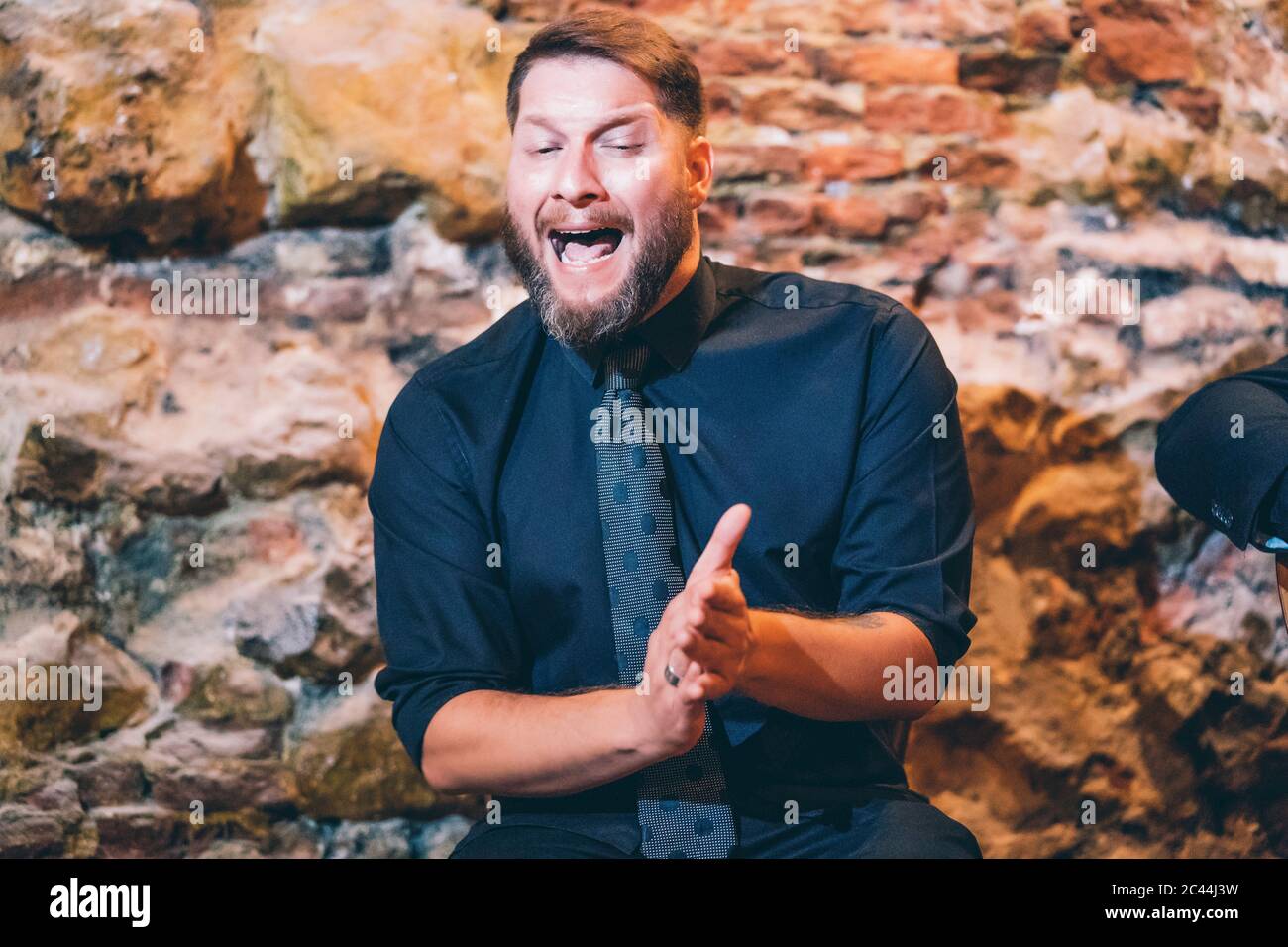 Bearded singer clapping hands while singing against wall in club Stock ...