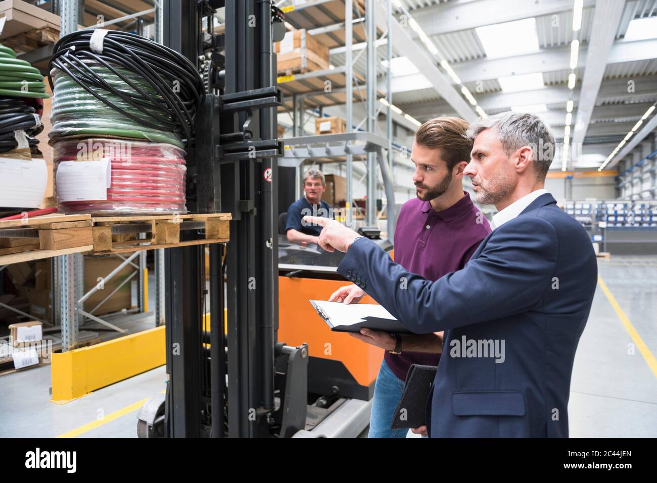 Two men and worker on forklift in high rack warehouse Stock Photo - Alamy