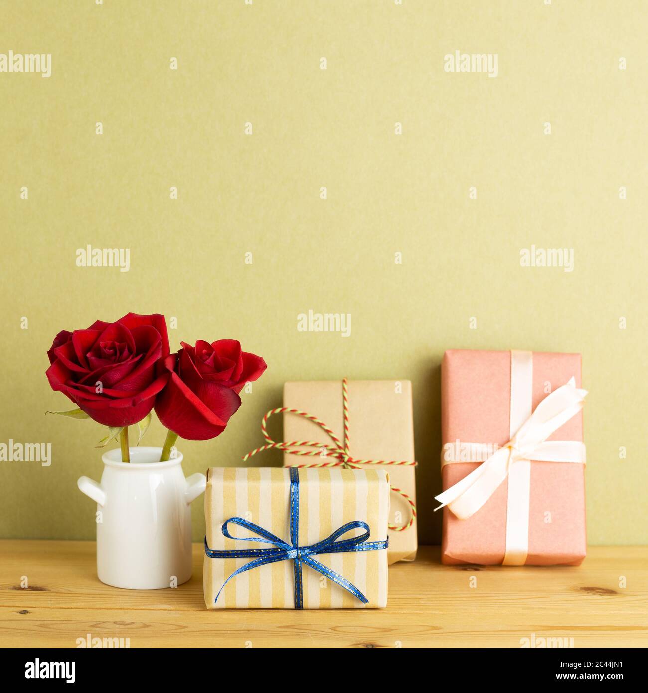 Gift boxes with red rose flowers in vase on wooden table with khaki ...