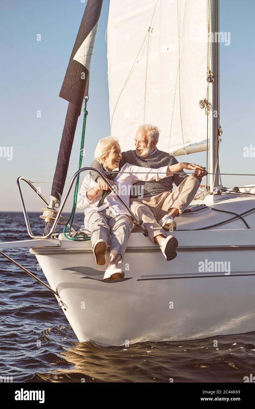 Sailing is a fun. A happy senior couple sitting on the side of a sail ...