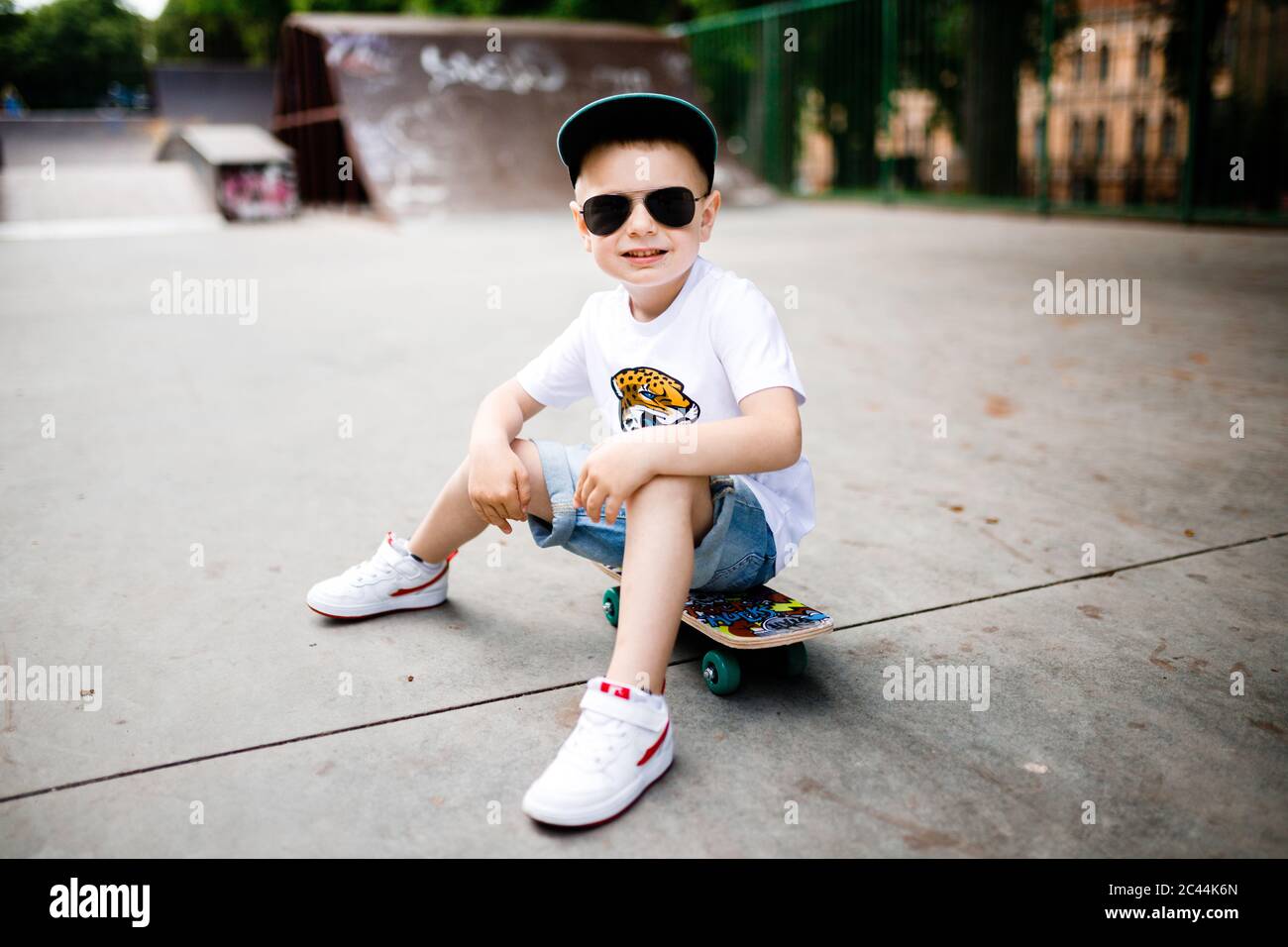 Boy with a skate in a skate park. The boy is sitting on a skateboard ...