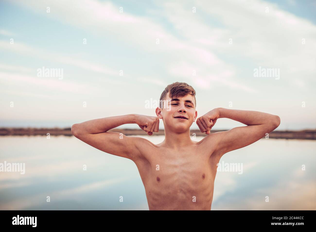 Smiling shirtless teenage boy flexing muscles looking away while ...