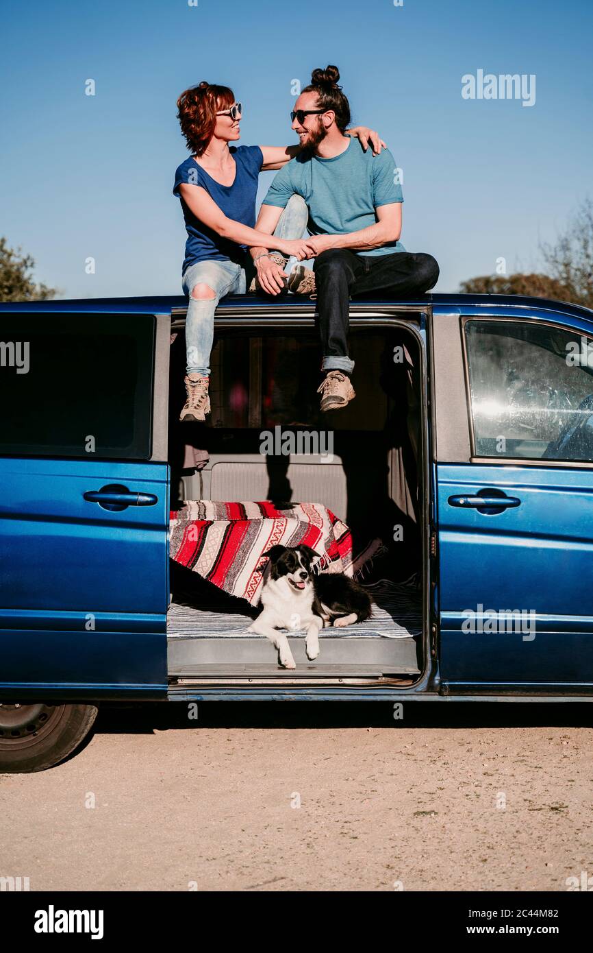 Happy couple sitting on the roof of a minivan Stock Photo - Alamy