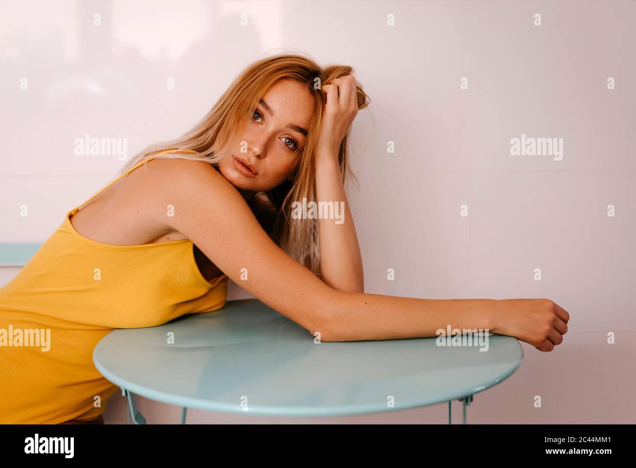 Beautiful woman leaning on table with hand in hair at home Stock Photo ...