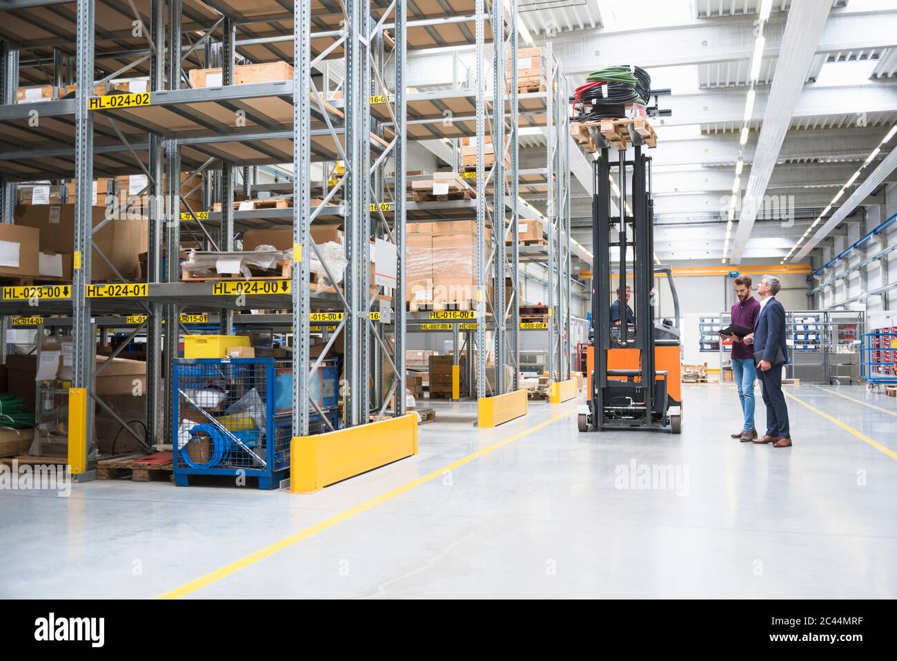 Two men and worker on forklift in high rack warehouse Stock Photo - Alamy
