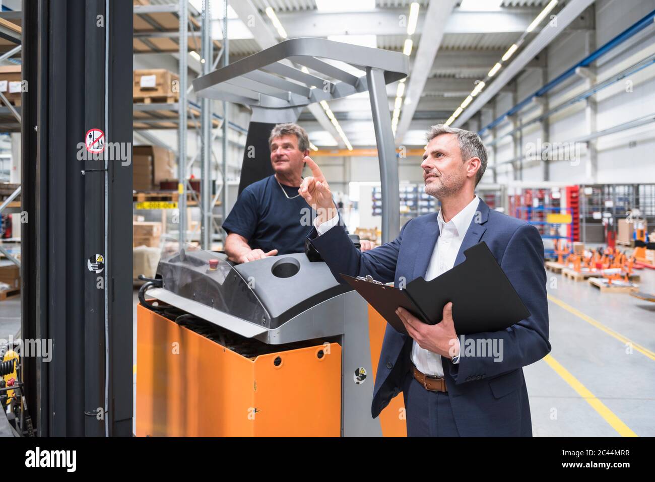 Businessman instructing worker on forklift in high rack warehouse Stock ...