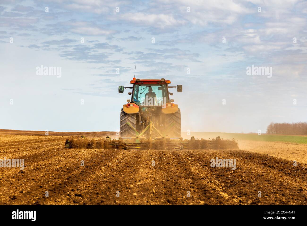 Back view of farmer in tractor plowing field in spring Stock Photo - Alamy