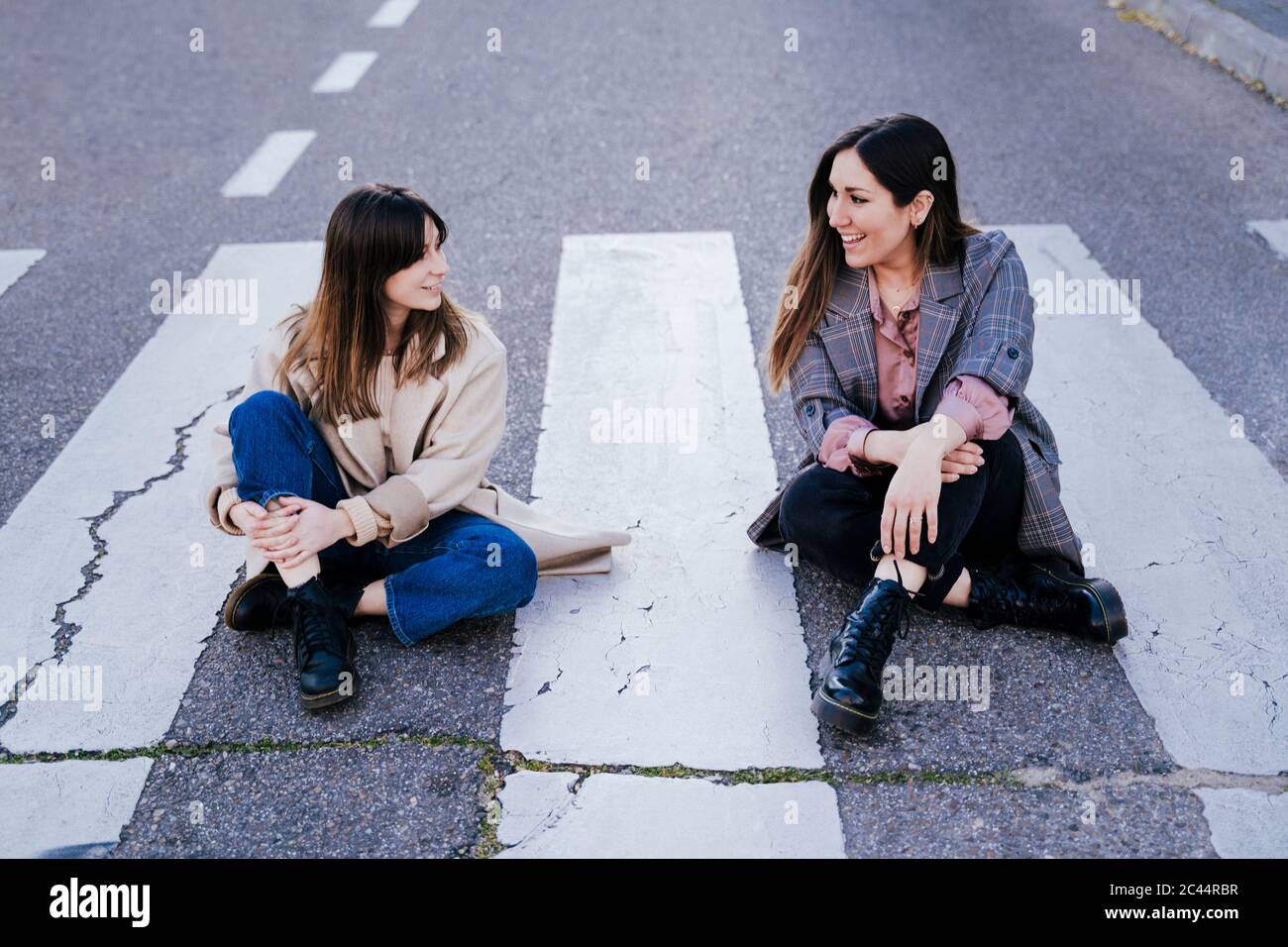 Two women sitting together on zebra crossing Stock Photo - Alamy