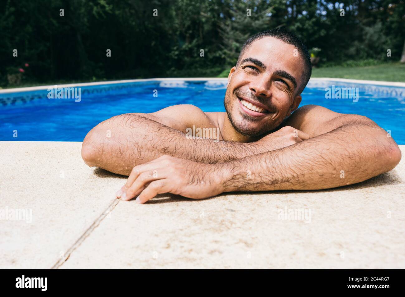 Smiling handsome wet young man looking away while relaxing in swimming ...