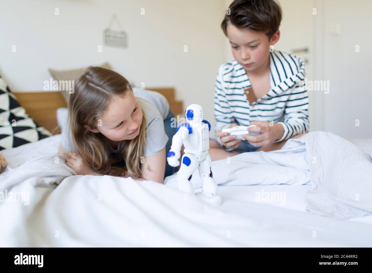 Brother and sister crouching on bed playing with toy robot Stock Photo ...