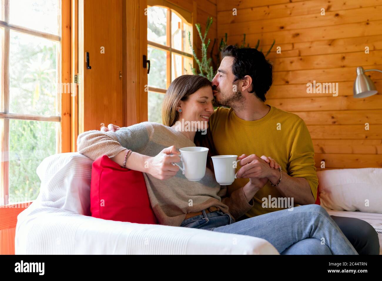 Romantic boyfriend holding coffee mug kissing on woman's forehead while ...