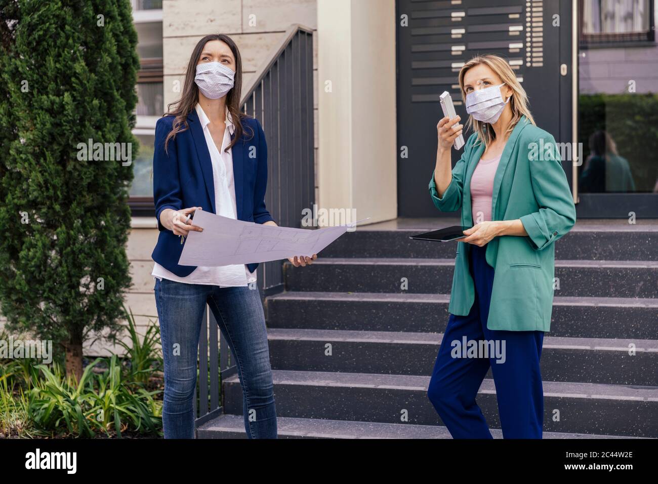 Two real estate agents wearing face masks while inspection outdoor area ...