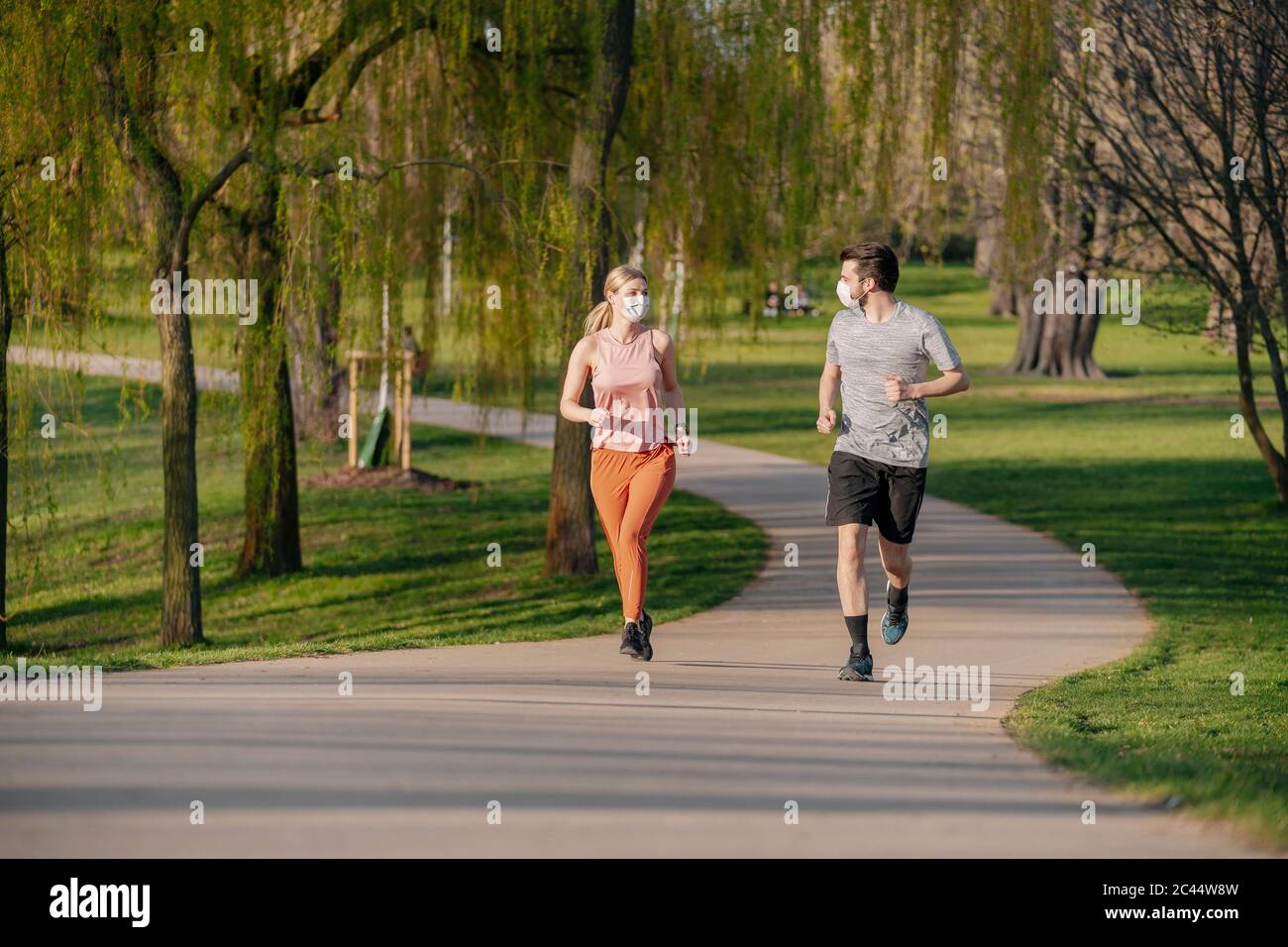 Couple wearing face masks while running on footpath at park Stock Photo ...